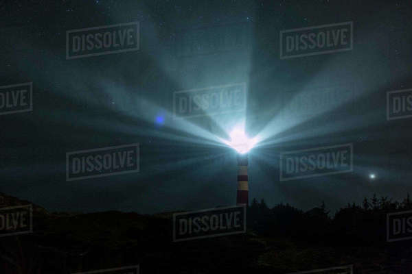 Light beacons illuminating from lighthouse under starry night sky ...