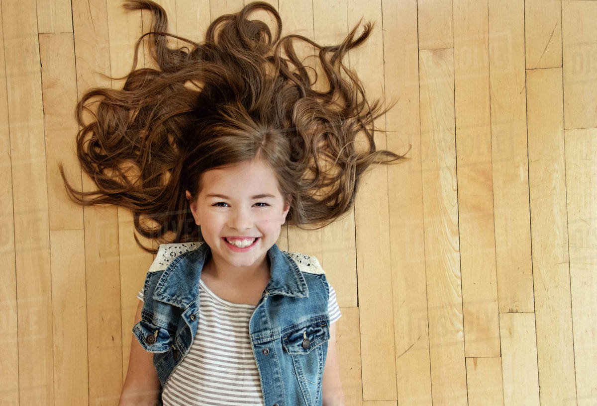 Portrait carefree girl with long brown hair laying on hardwood floor ...