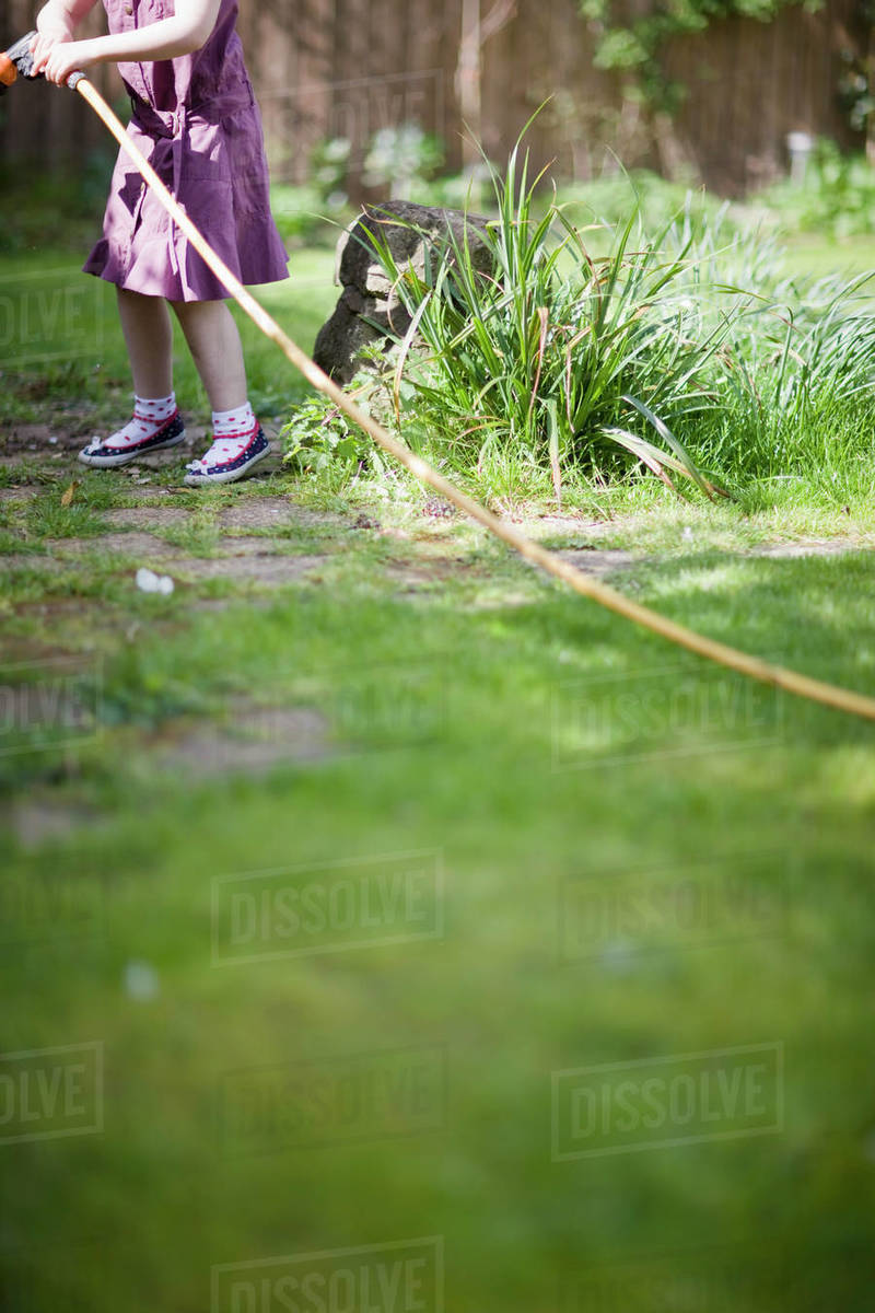 Headless young girl pulling garden hose - Stock Photo - Dissolve