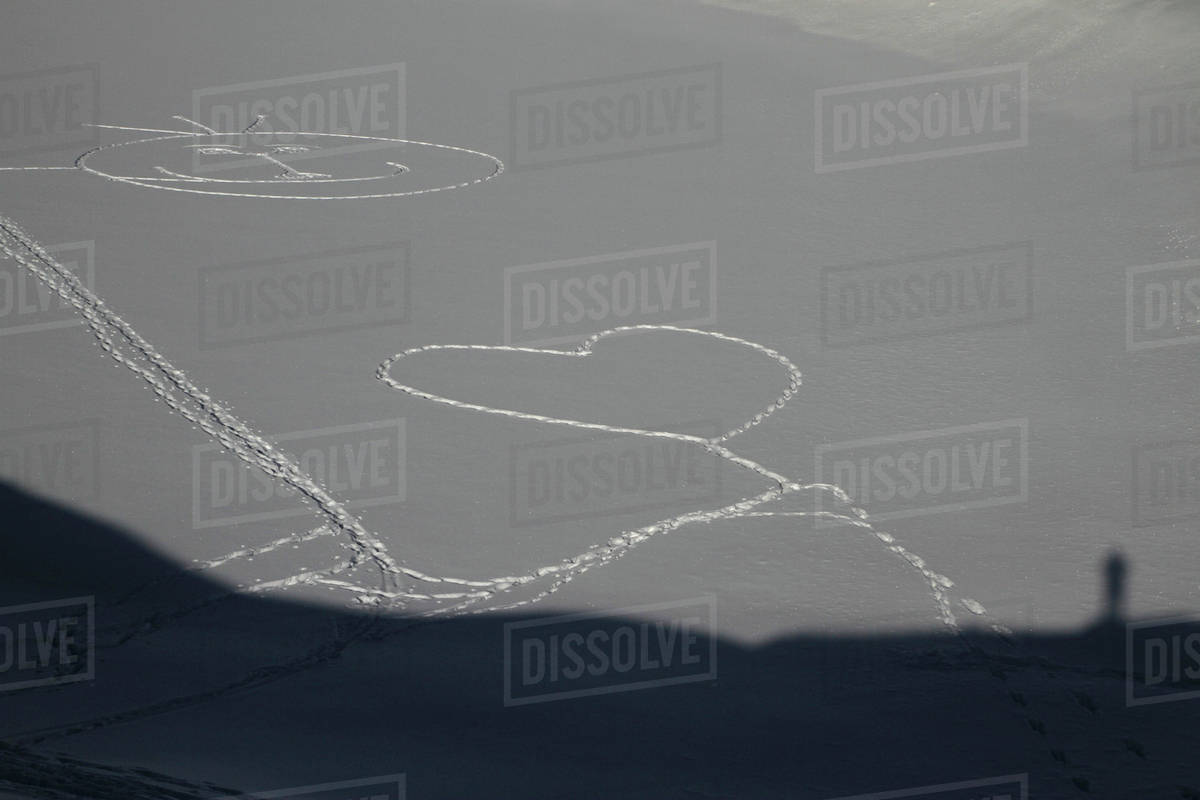 A heart shape and smiley face stamped out in the snow by footprints ...