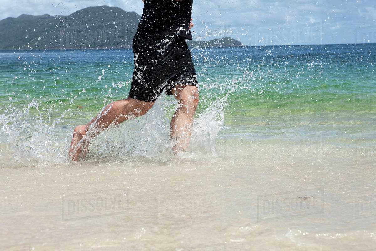 Low section of a man running through the water at a beach - Royalty ...