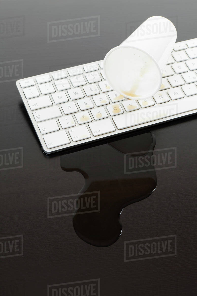A cup of soda spilled on a computer keyboard - Stock Photo - Dissolve