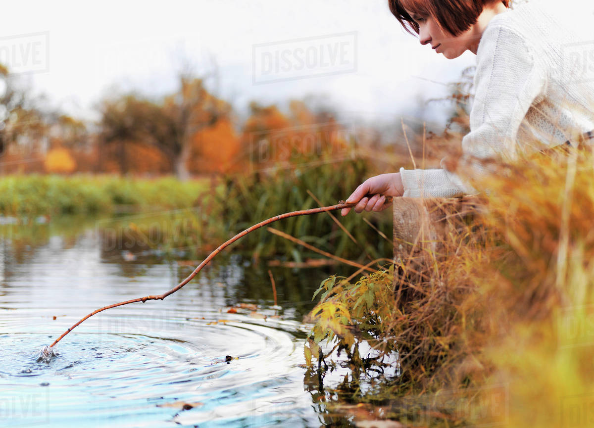 A woman poking at the water with a stick - Stock Photo - Dissolve